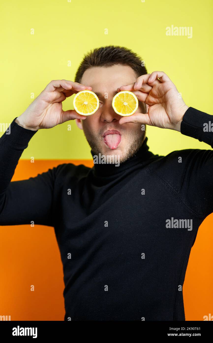 Portrait of a man on a yellow background in black raglan with cut lemon ...