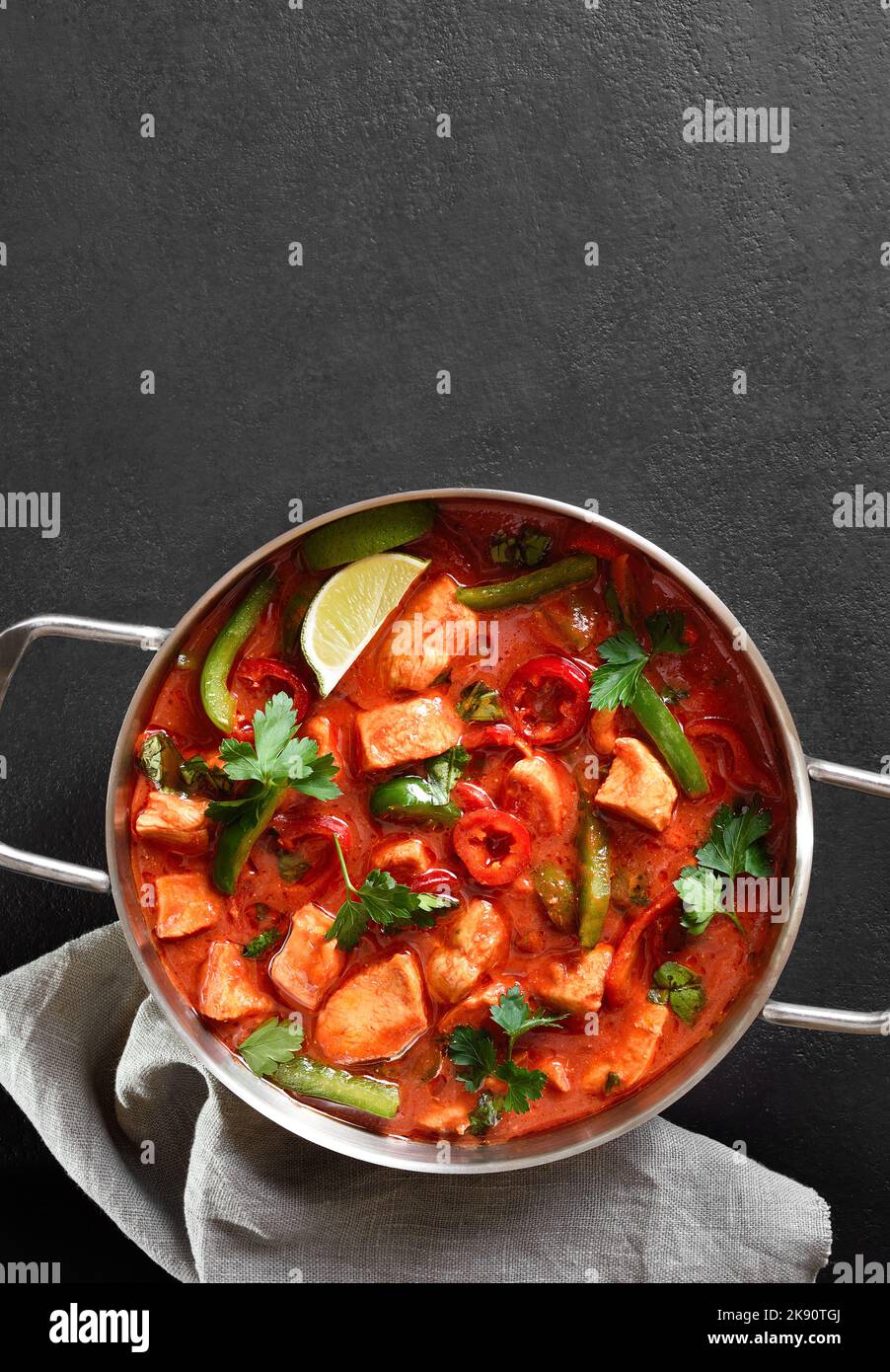 Thai style red chicken curry with vegetables in pan over black stone ...