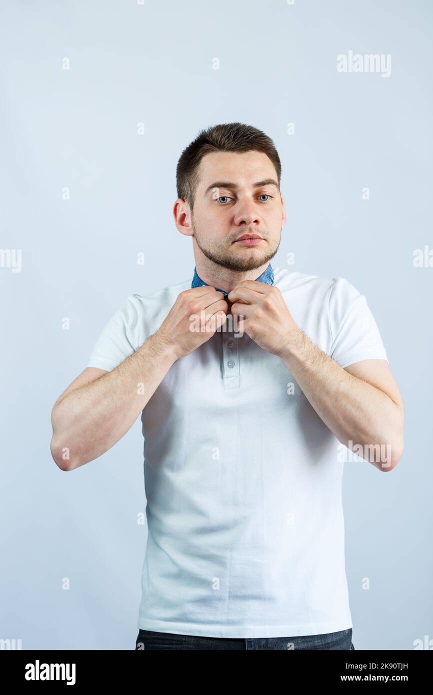 A man fastens a button on his white polo. he is on a white background ...