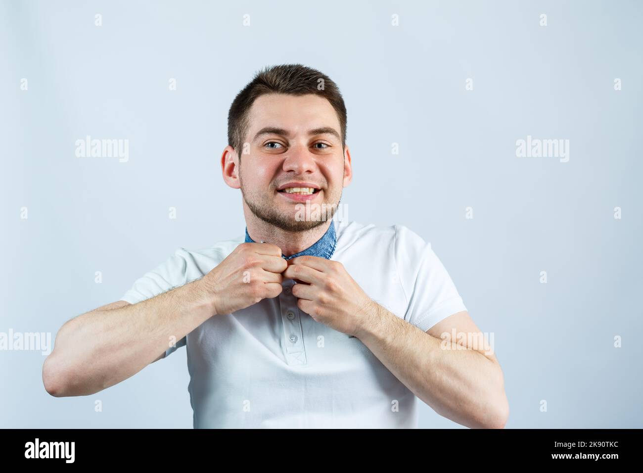 A man fastens a button on his white polo. he is on a white background ...