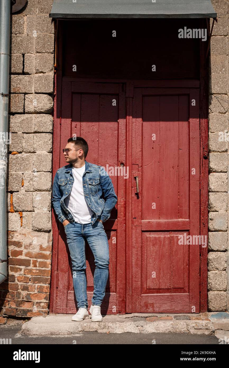 Handsome man with a beard in a denim jacket and denim pants stands near ...