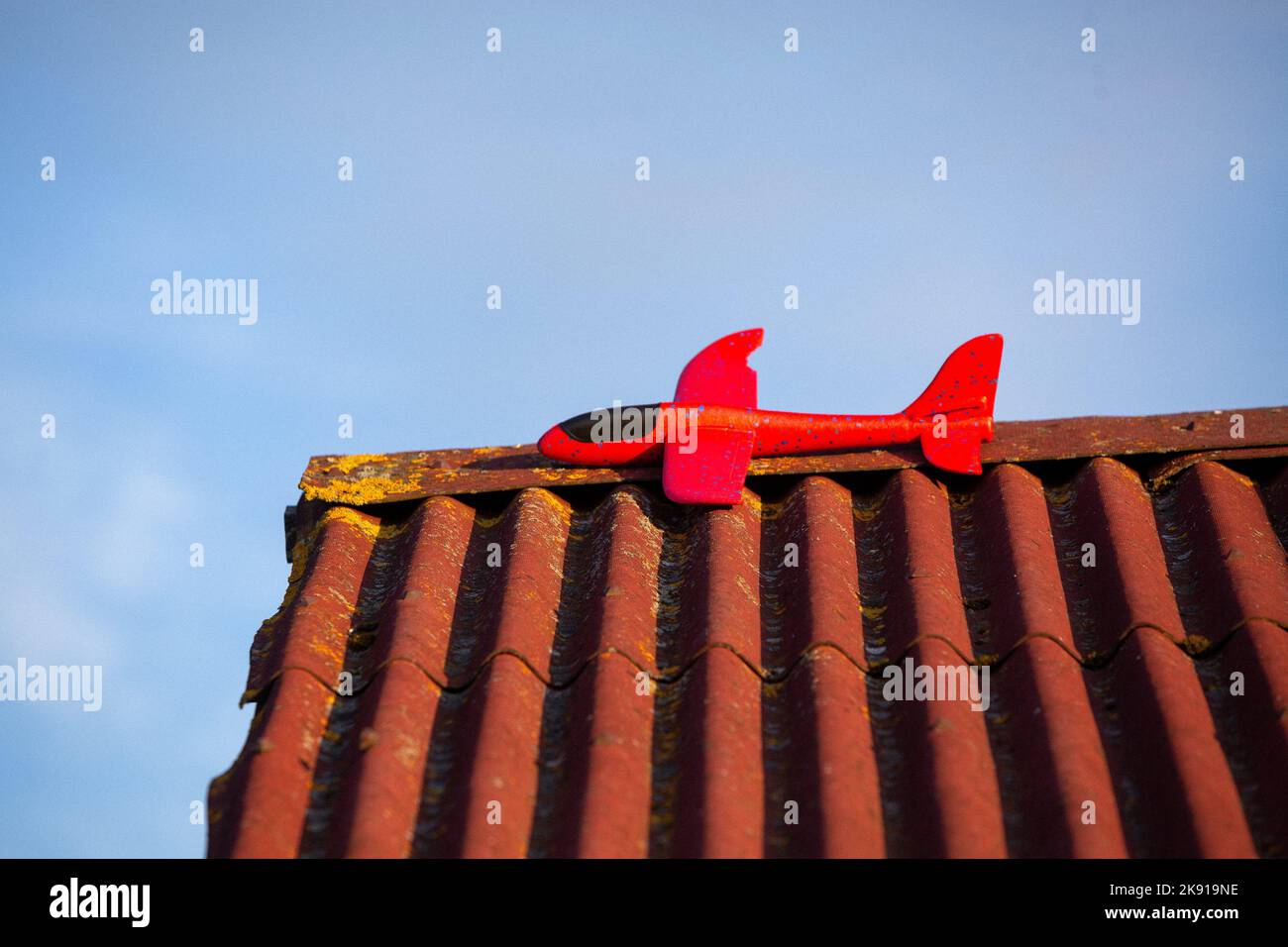 A red foam glider airplane toy landed on a roof against a blue sky ...