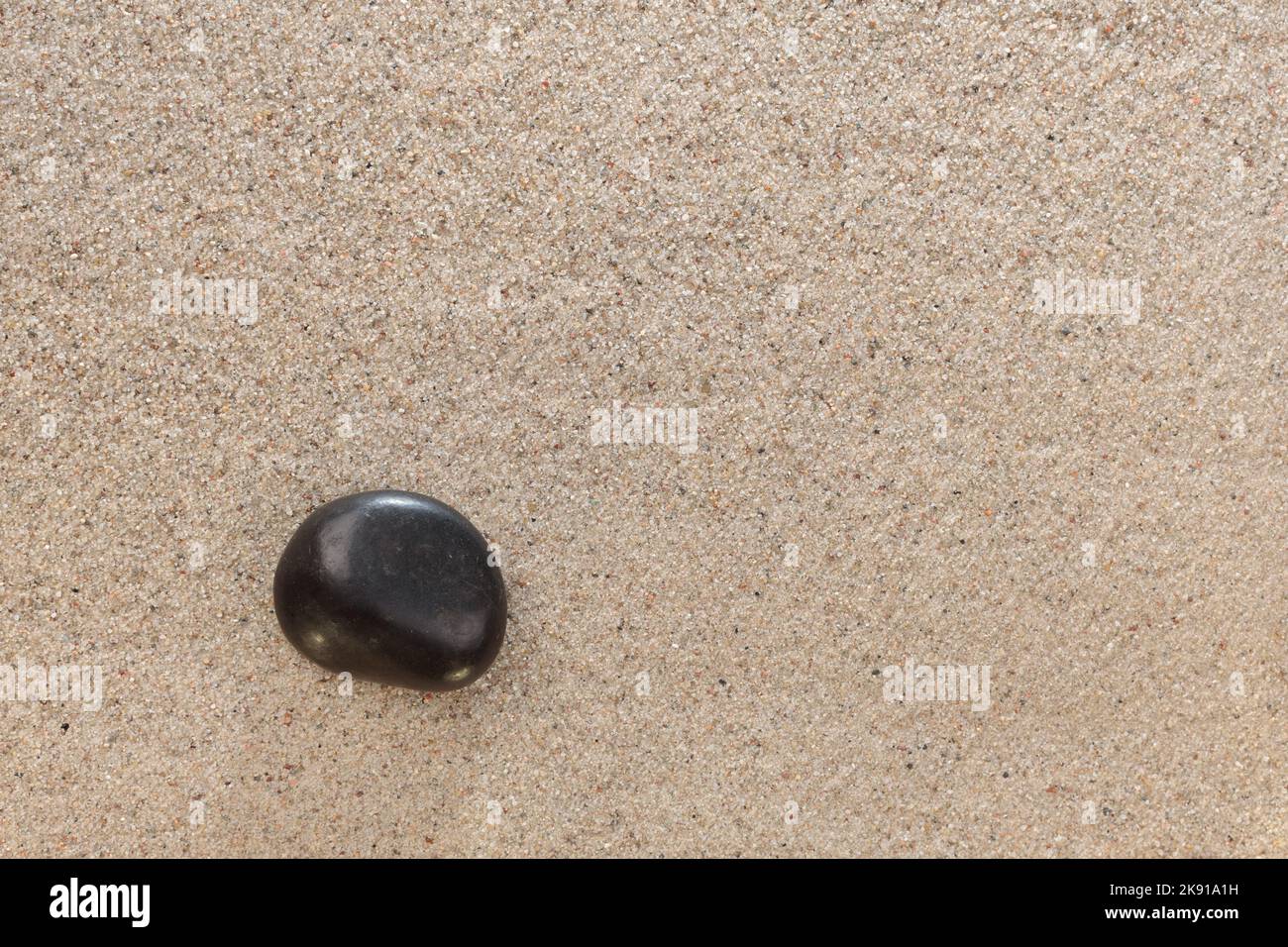 A black shiny stone in the sand Stock Photo - Alamy