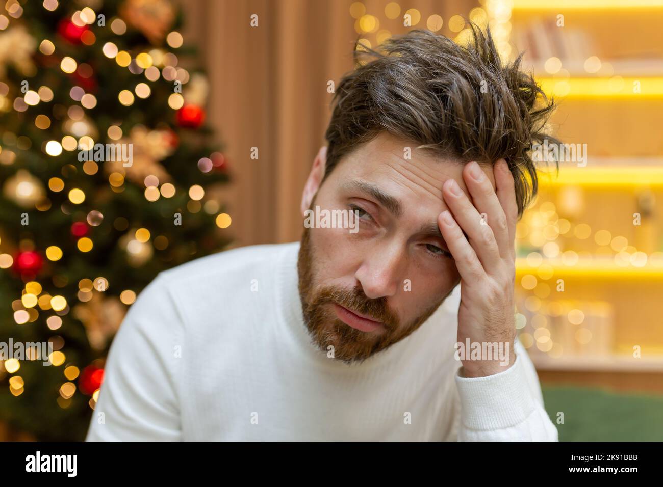 Sad depressed man at home sitting on sofa near Christmas tree, man ...