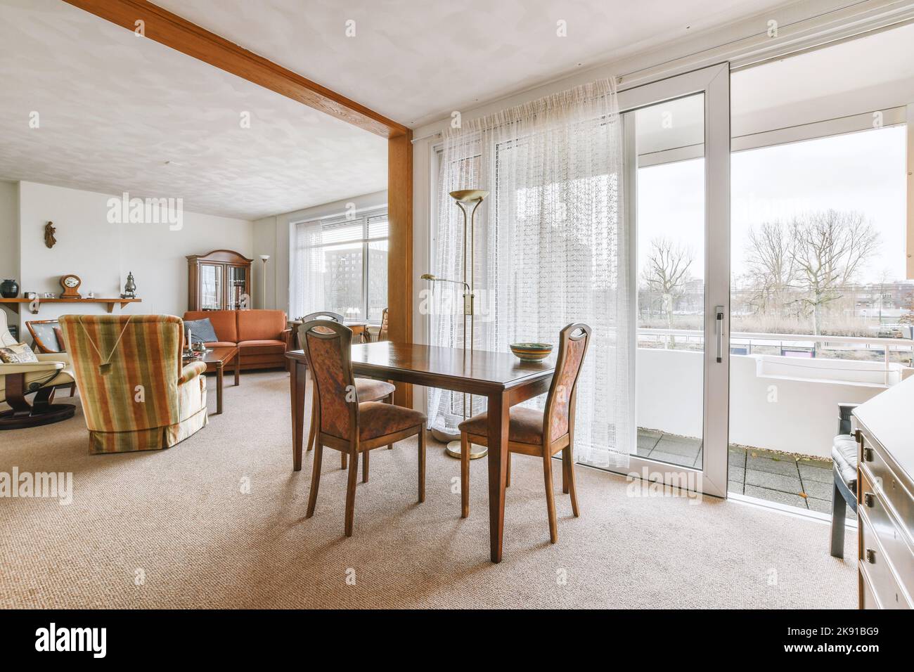 Wooden table with vase and chairs placed near opened balcony door in ...
