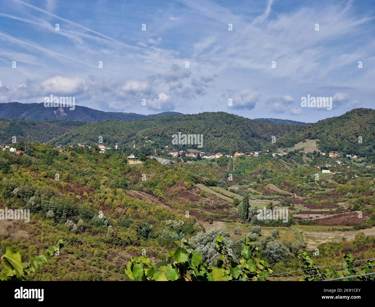 A scenic view of a green landscape with forested hills under a blue sky ...