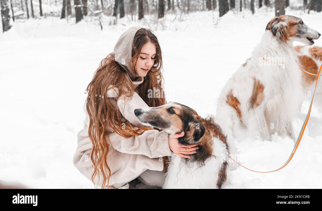 Young beautiful girl in snowy cold winter frost forest walking with pet ...