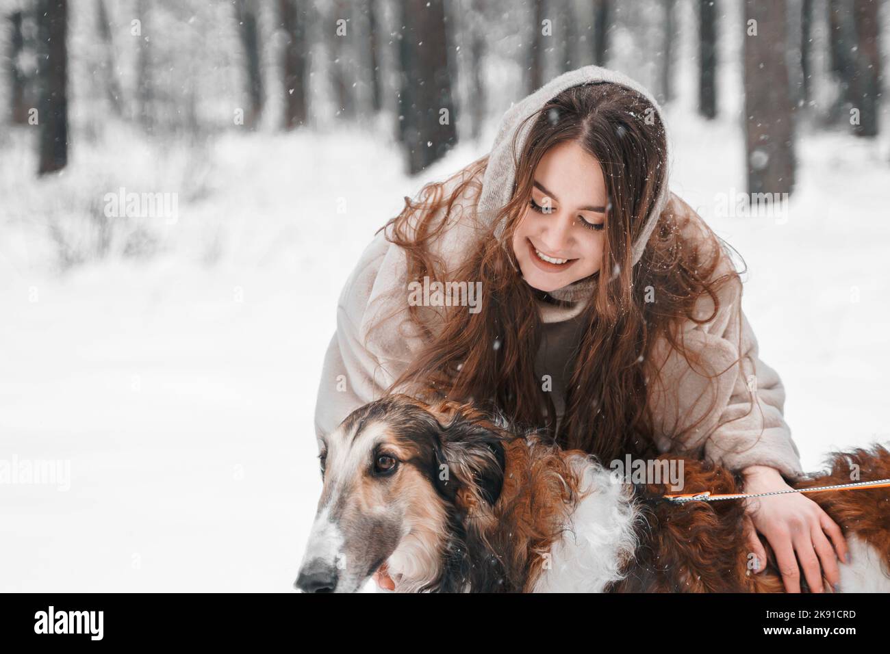 Young beautiful girl in snowy cold winter frost forest walking with pet ...