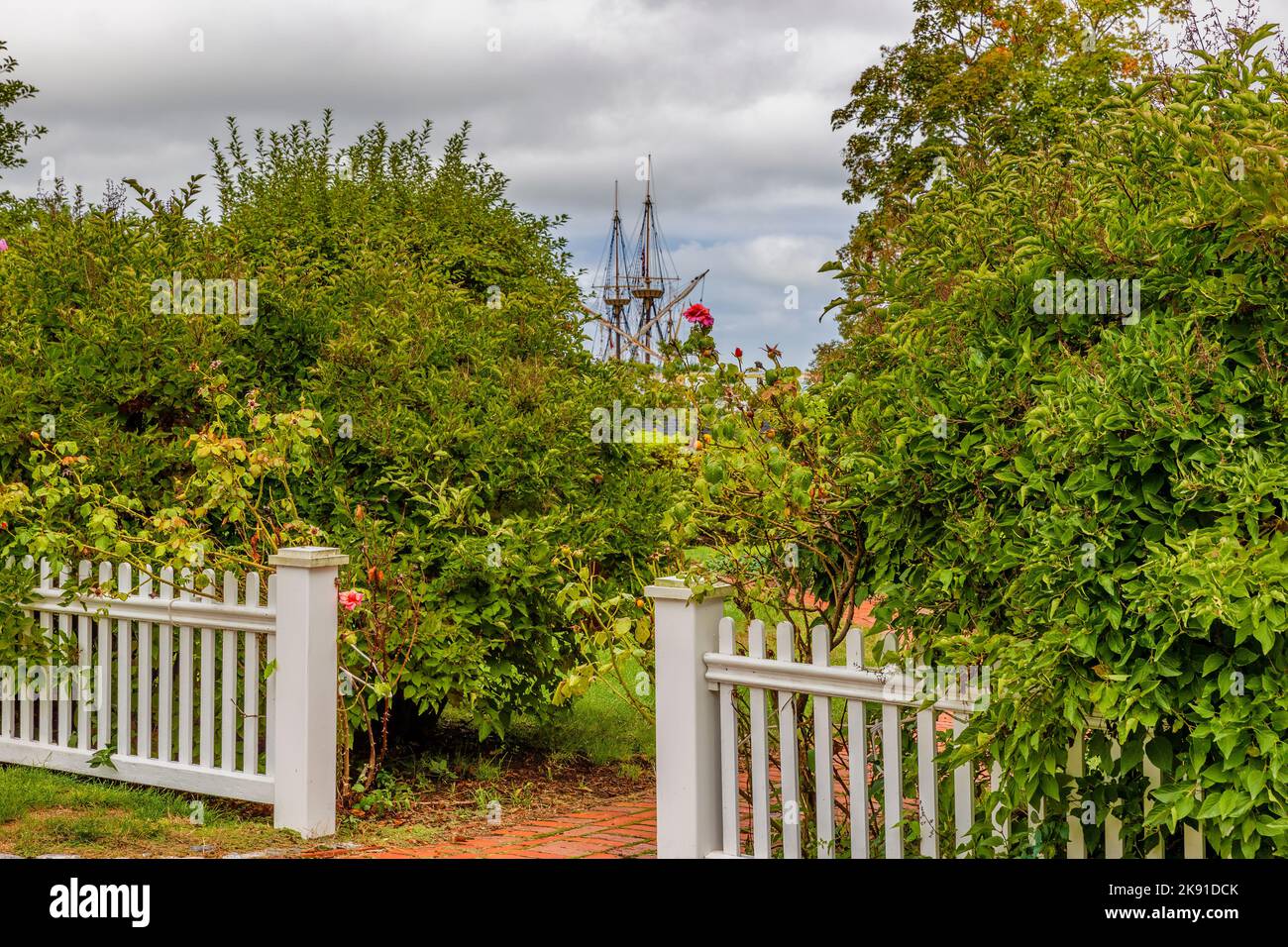 A open path through a white fence from the sidewalk shows a glimpse the ...