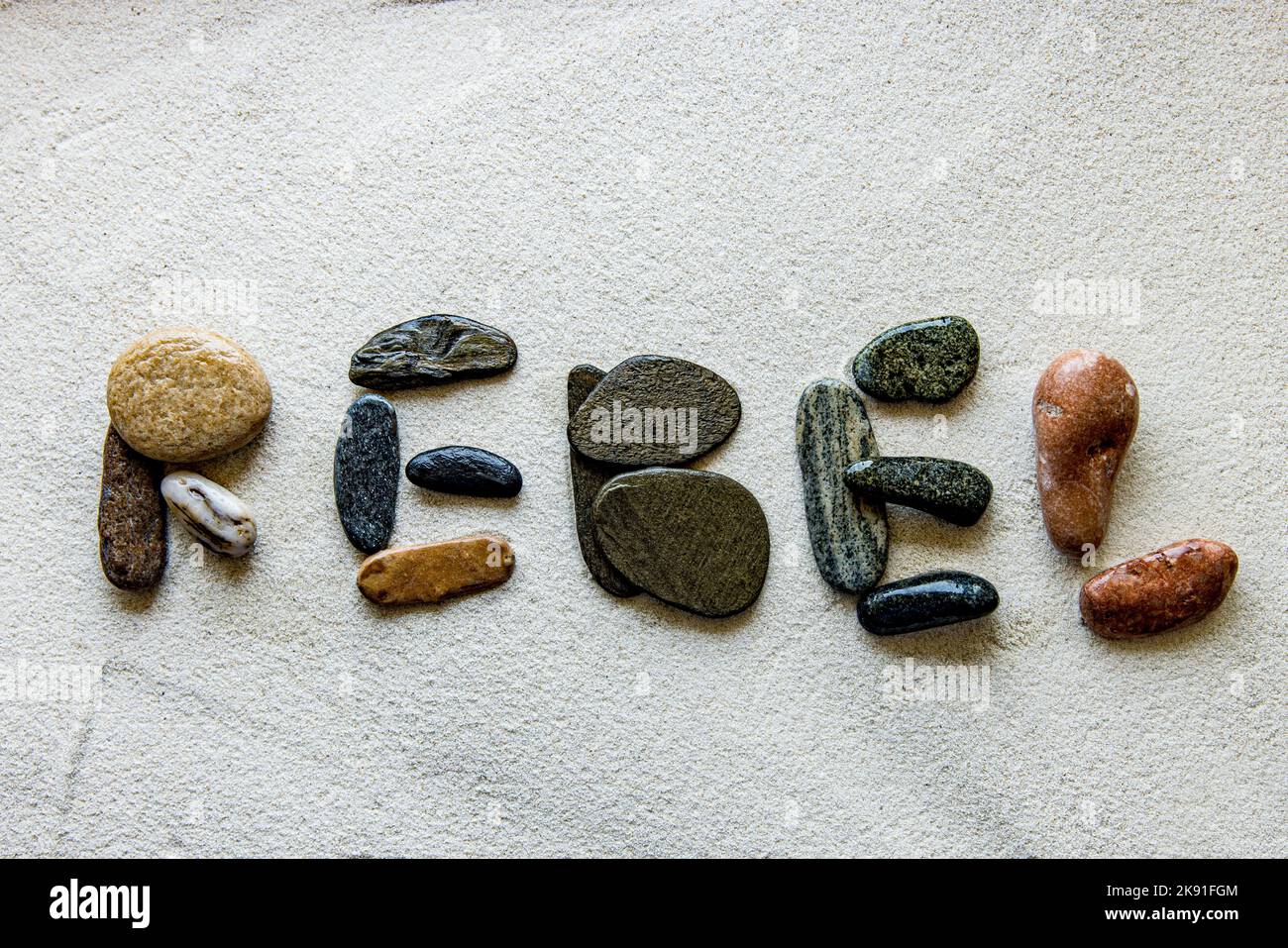 The word: REBEL, written using colored stones on white sand Stock Photo ...