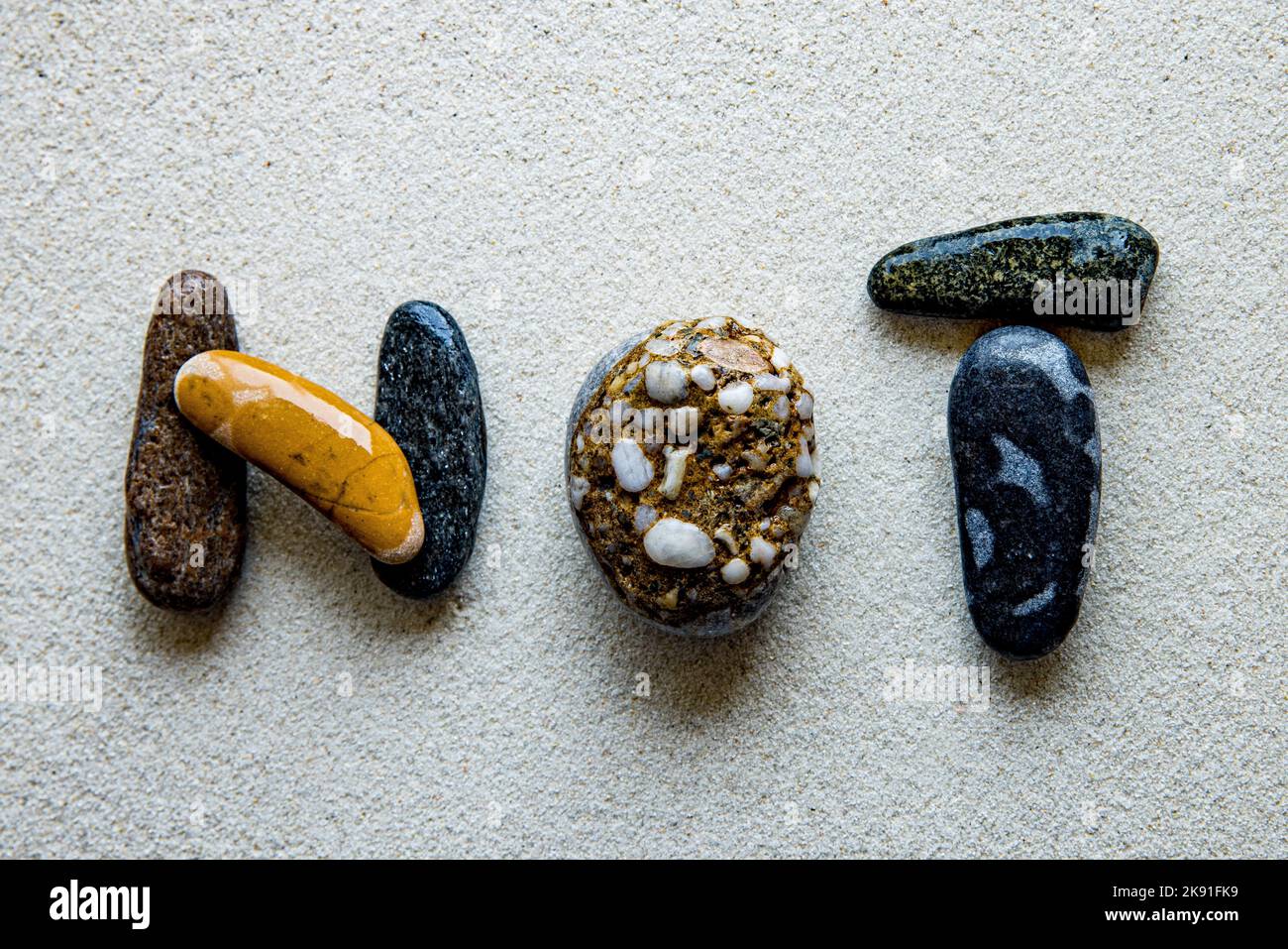 The word: NOT, written using colored stones on white sand Stock Photo ...