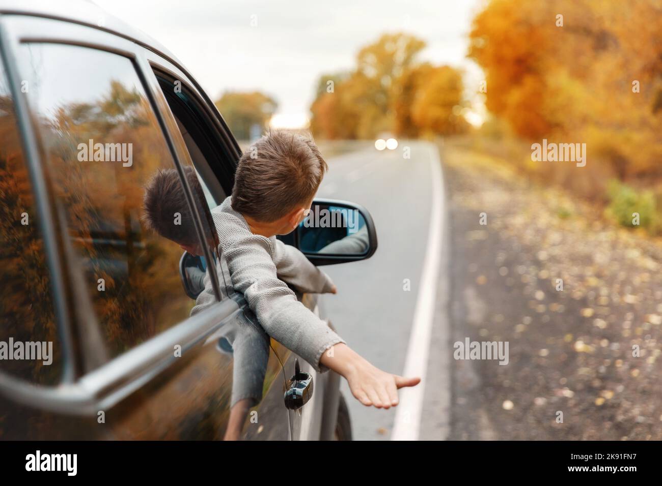 Boy putting his heads and hands out of the car window driving down a ...