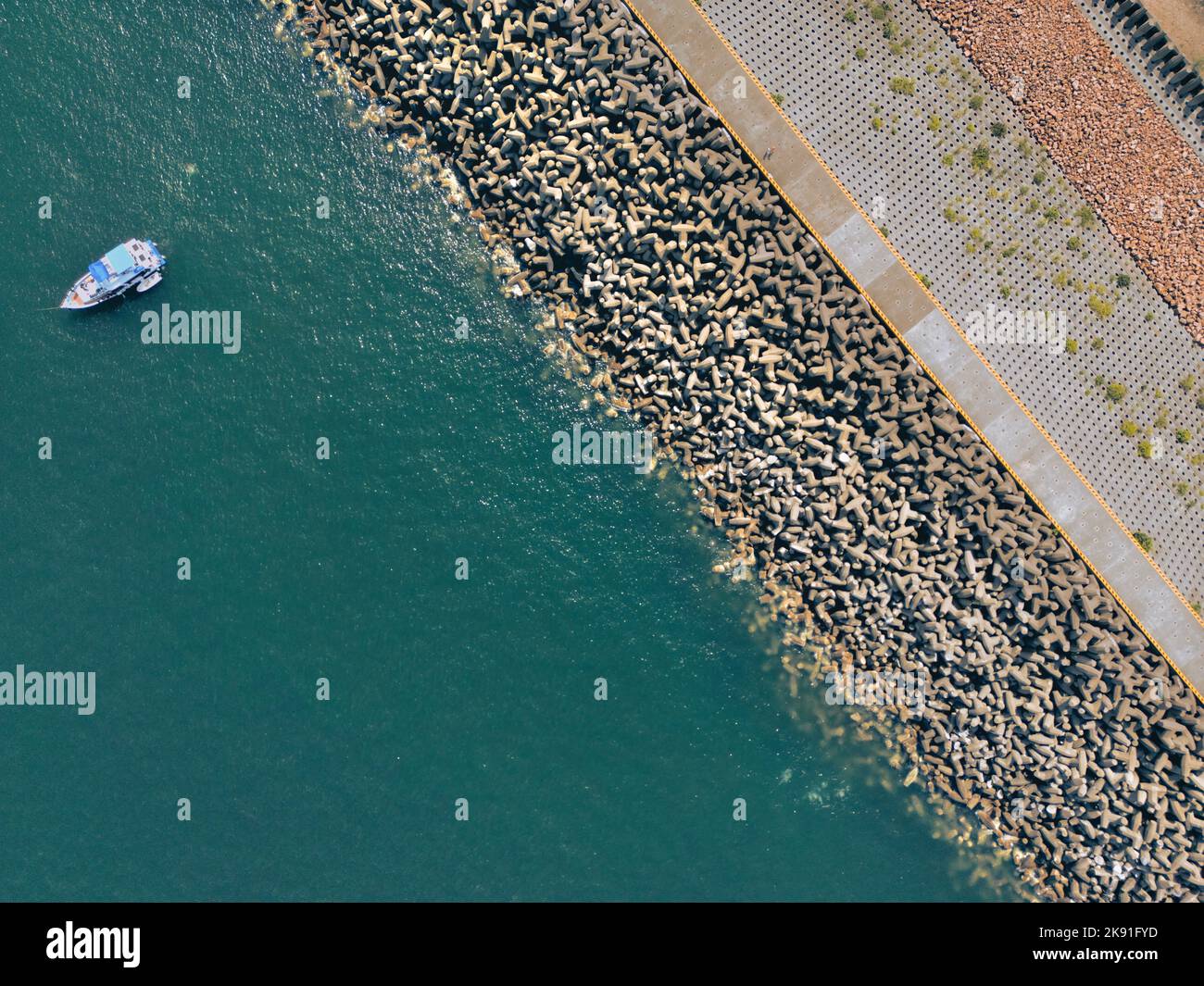 An aerial view of dolos blocks on the shore near the sea with a boat in ...