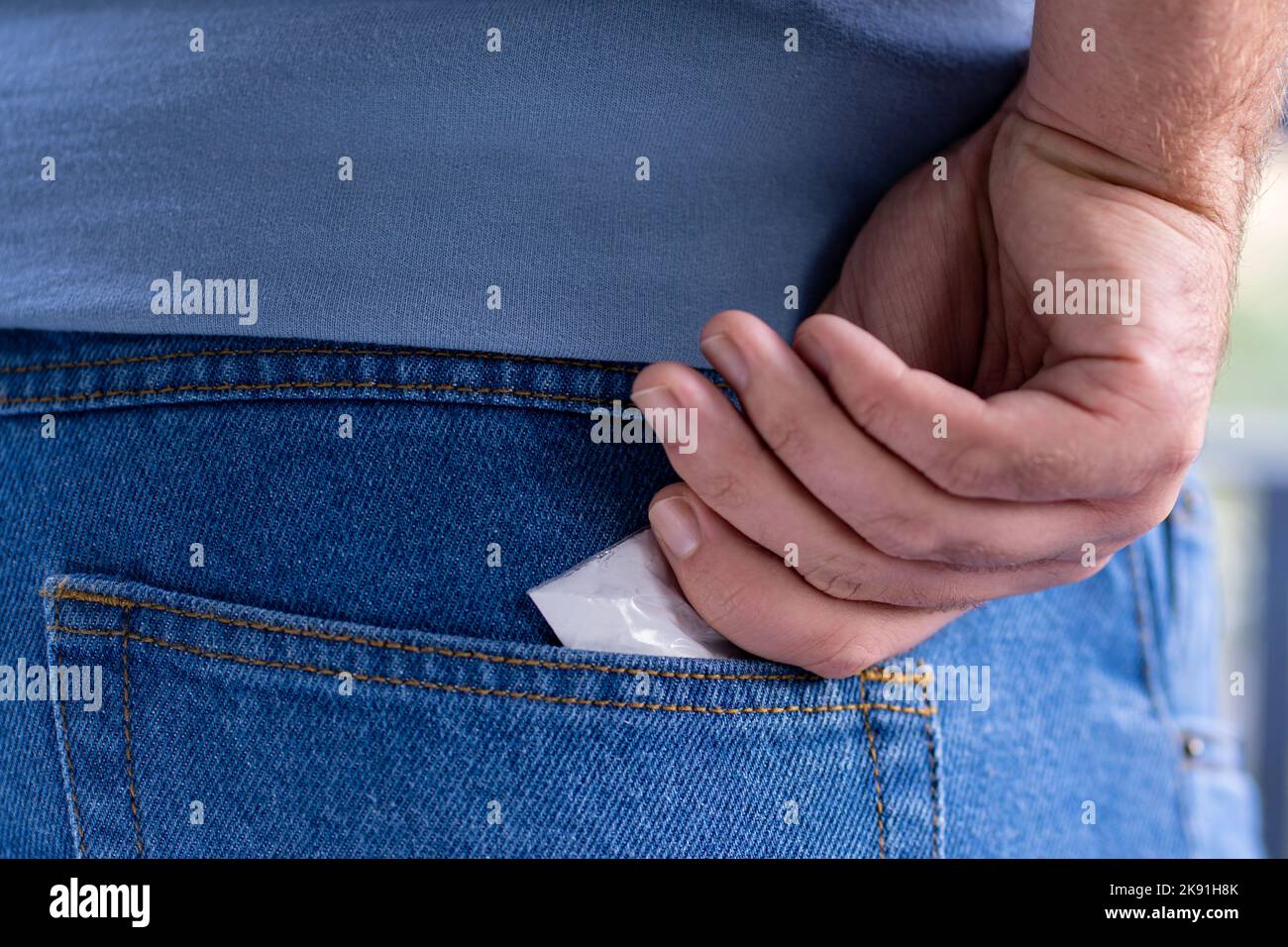 man's hand pulling a packet of drugs out of the back pocket of a pair ...