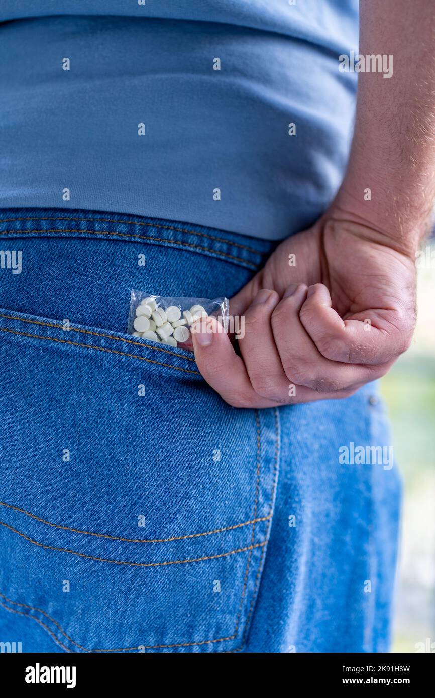 man's hand pulling a packet of white pills out of the back pocket of ...