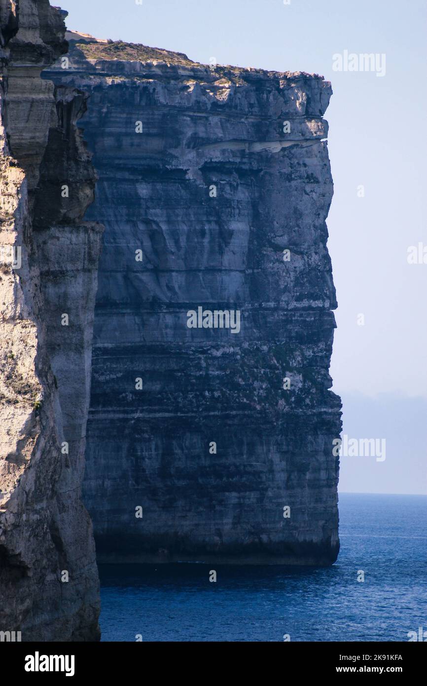 A vertical closeup of Ta Cenc cliffs near the blue sea, gloomy and ...