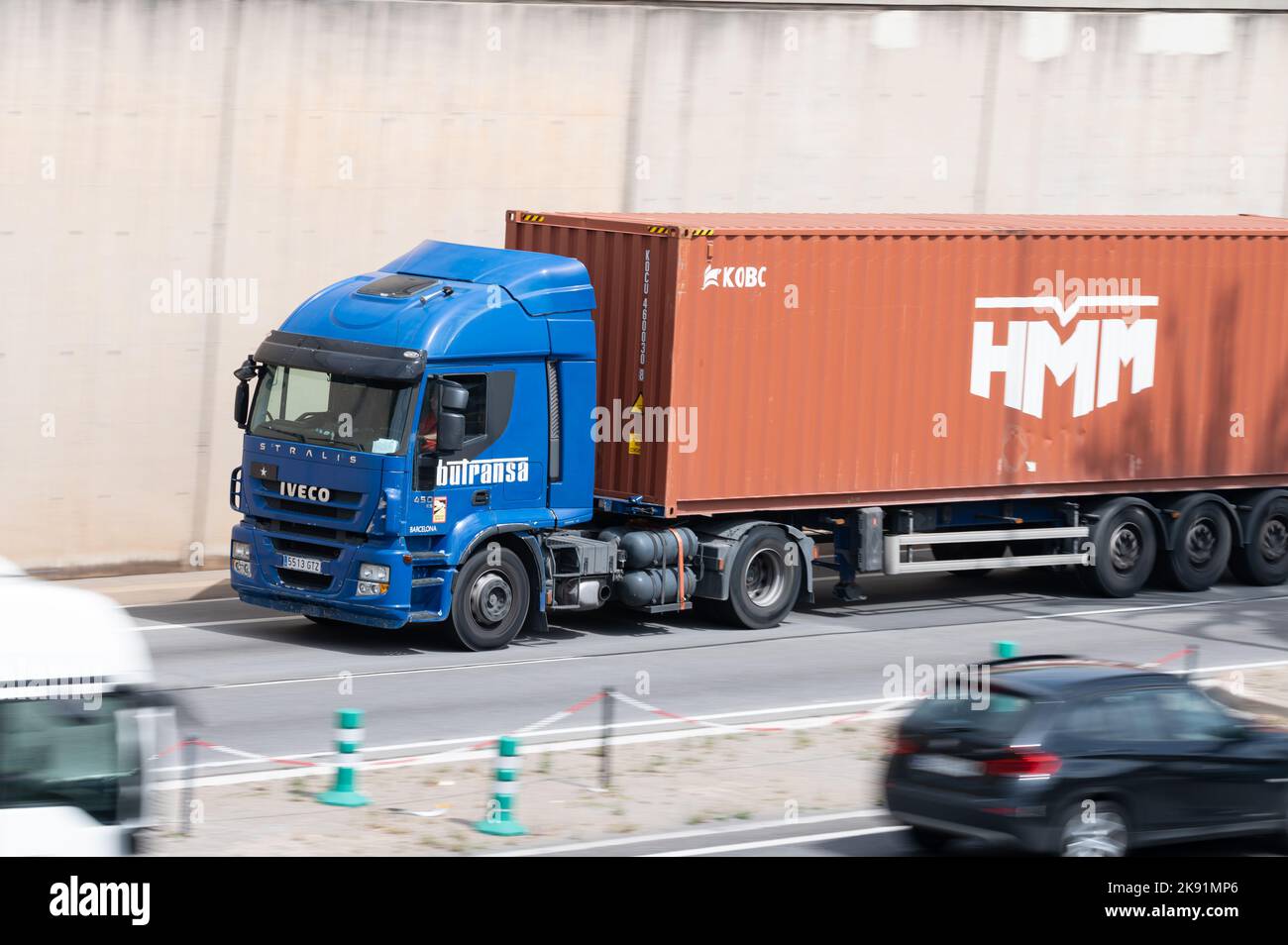 Blue Iveco Stralis truck loading a red container trailer along ...