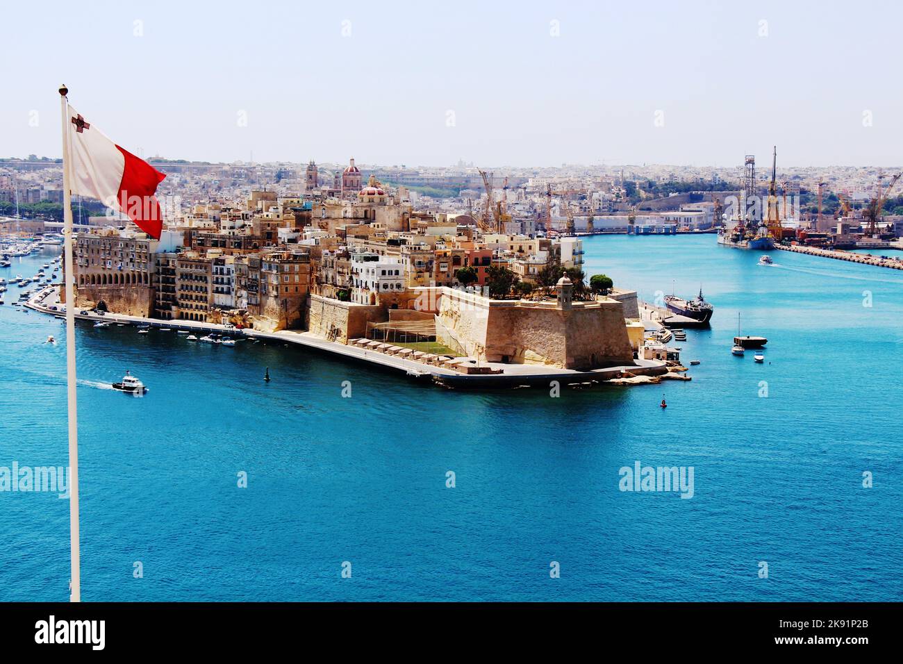 The flag of Malta and the old Forts, buildings with boats around in ...