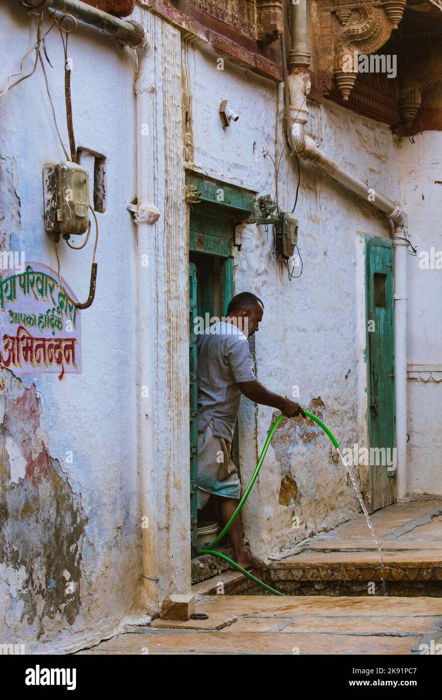 A vertical shot of a man standing outside his house holding a water ...