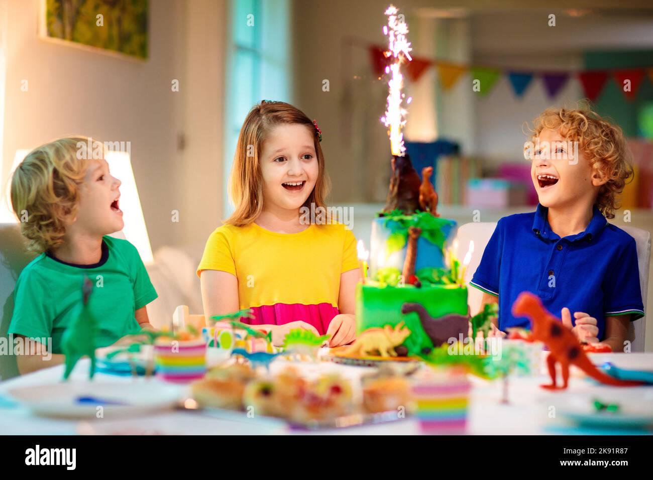 Kids birthday party. Dinosaur theme cake. Little girl blowing candles ...