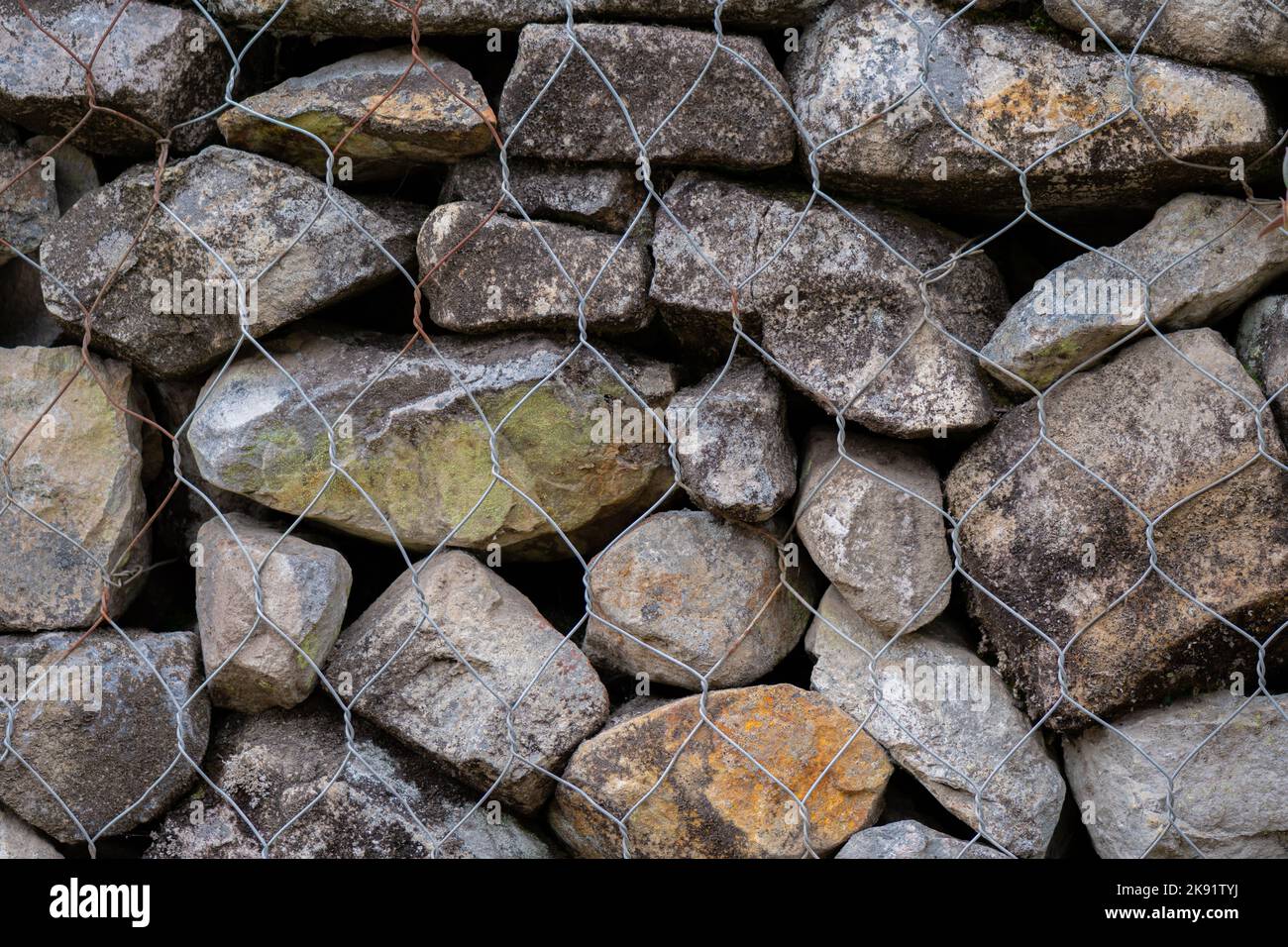 A wall with stacked rocks covered with metal net Stock Photo - Alamy