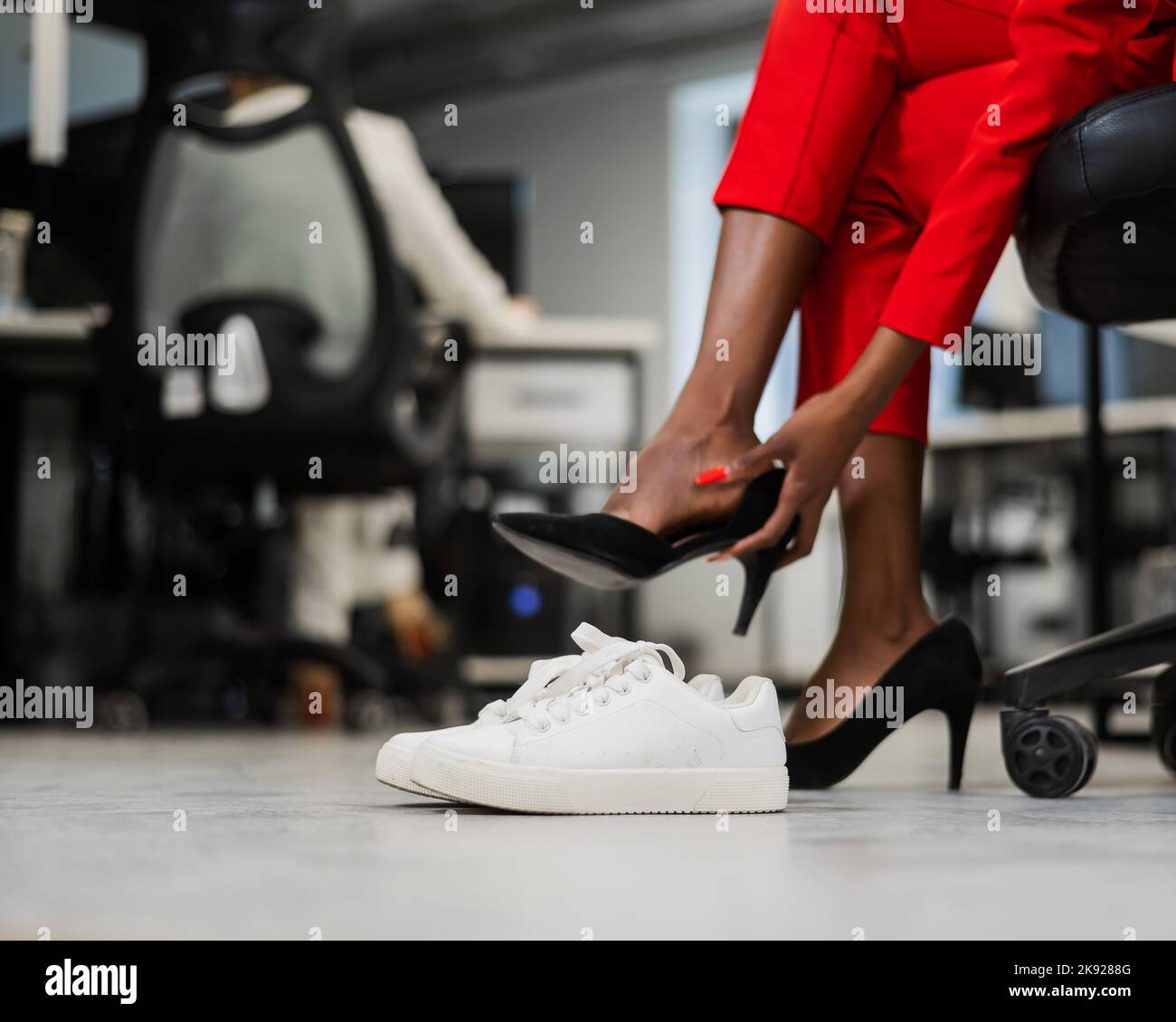 African woman changing from high heels to sneakers in the office. Tired ...