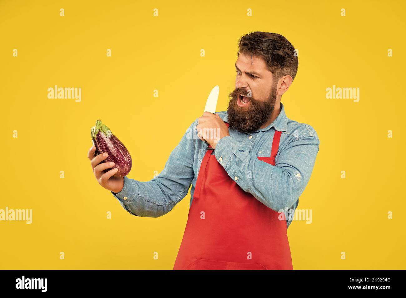 Angry man in apron holding cooks knife and eggplant yellow background ...