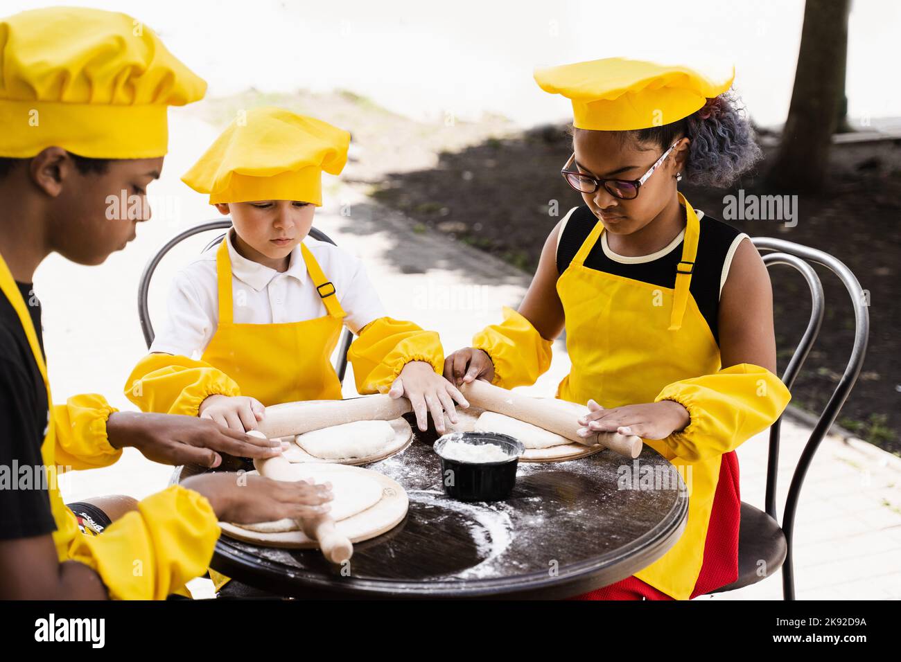 Multiethnic cooks children in yellow chefs hat and apron cooking dough ...