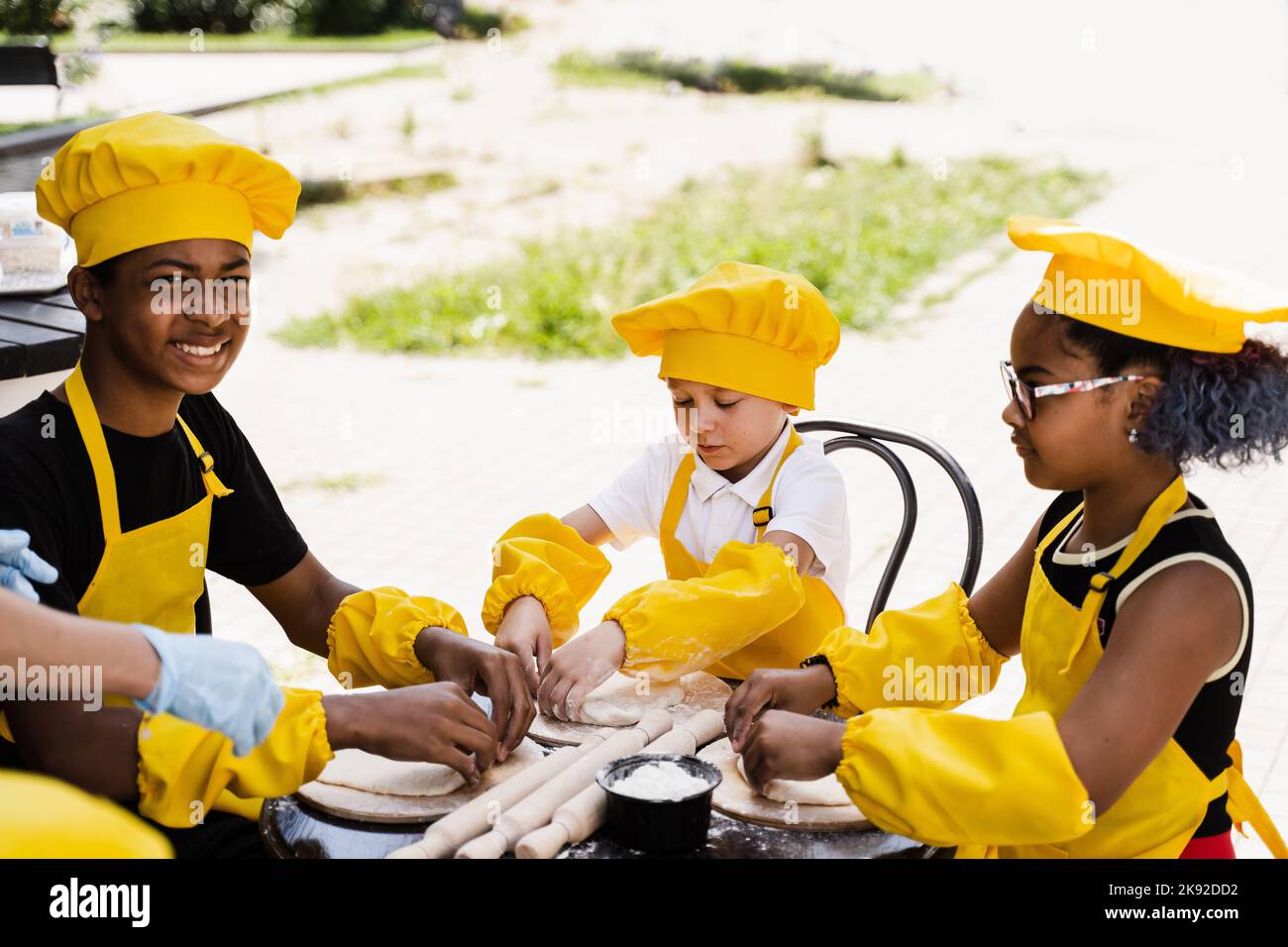 Multiethnic cooks children in yellow chefs hat and apron cooking dough ...
