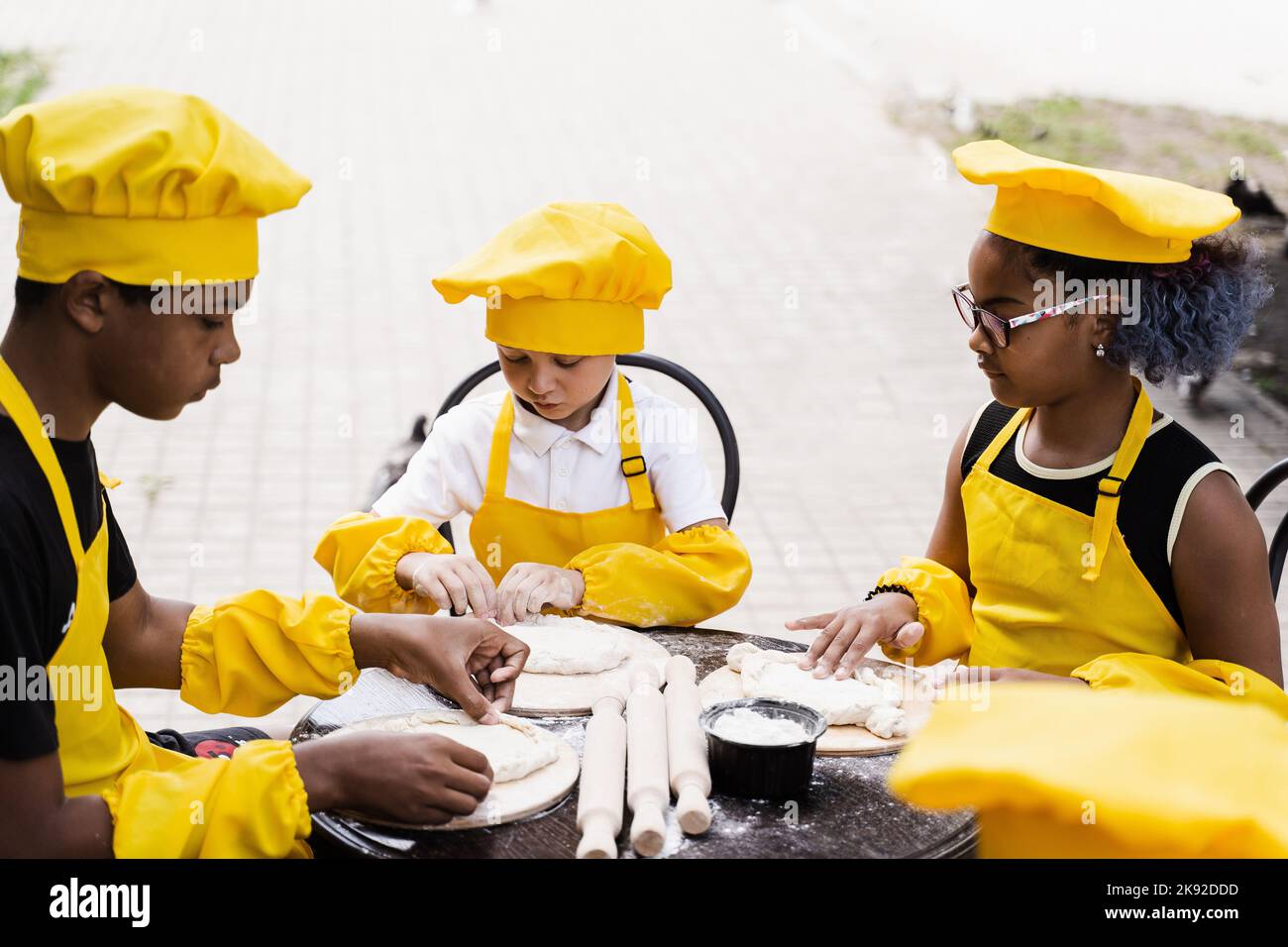 Multiethnic cooks children in yellow chefs hat and apron cooking dough ...
