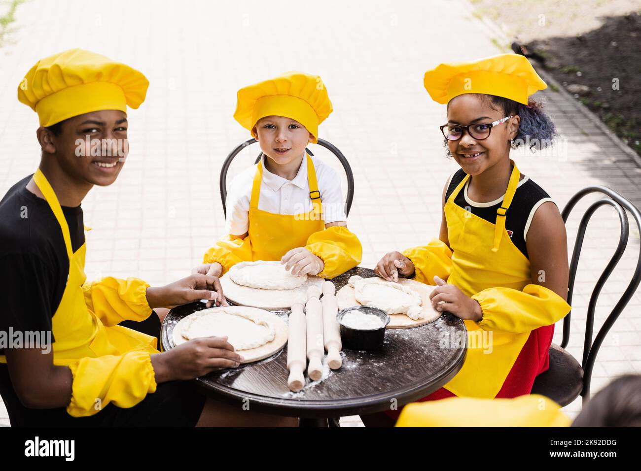 Multiethnic cooks children in yellow chefs hat and apron cooking dough ...