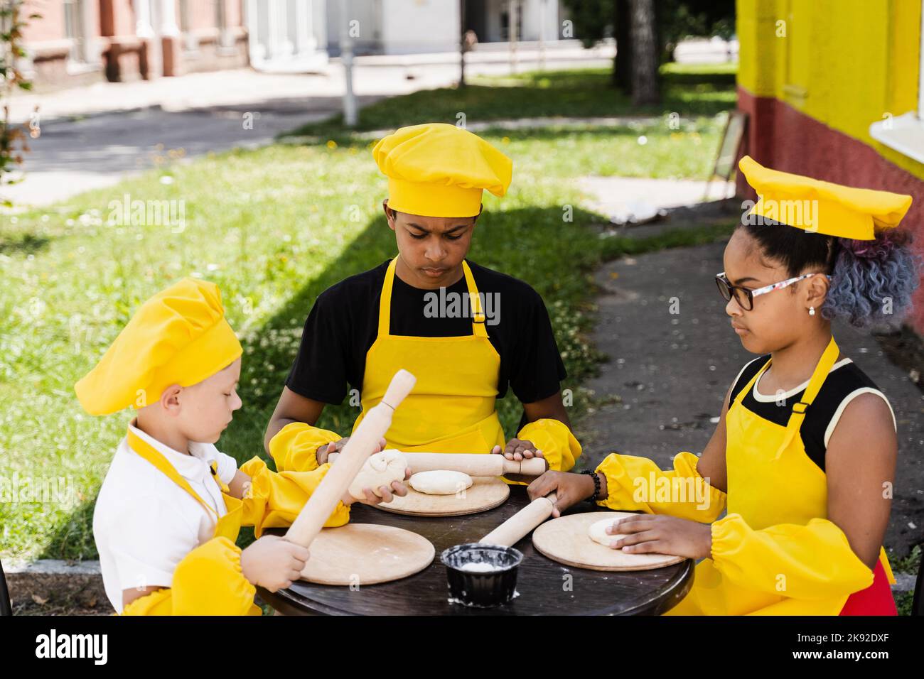 Multiracial cooks children in yellow chefs hat and apron cooking dough ...