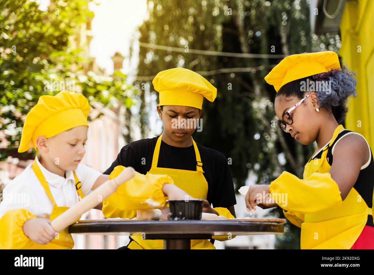 Multiracial cooks children in yellow chefs hat and apron cooking dough ...
