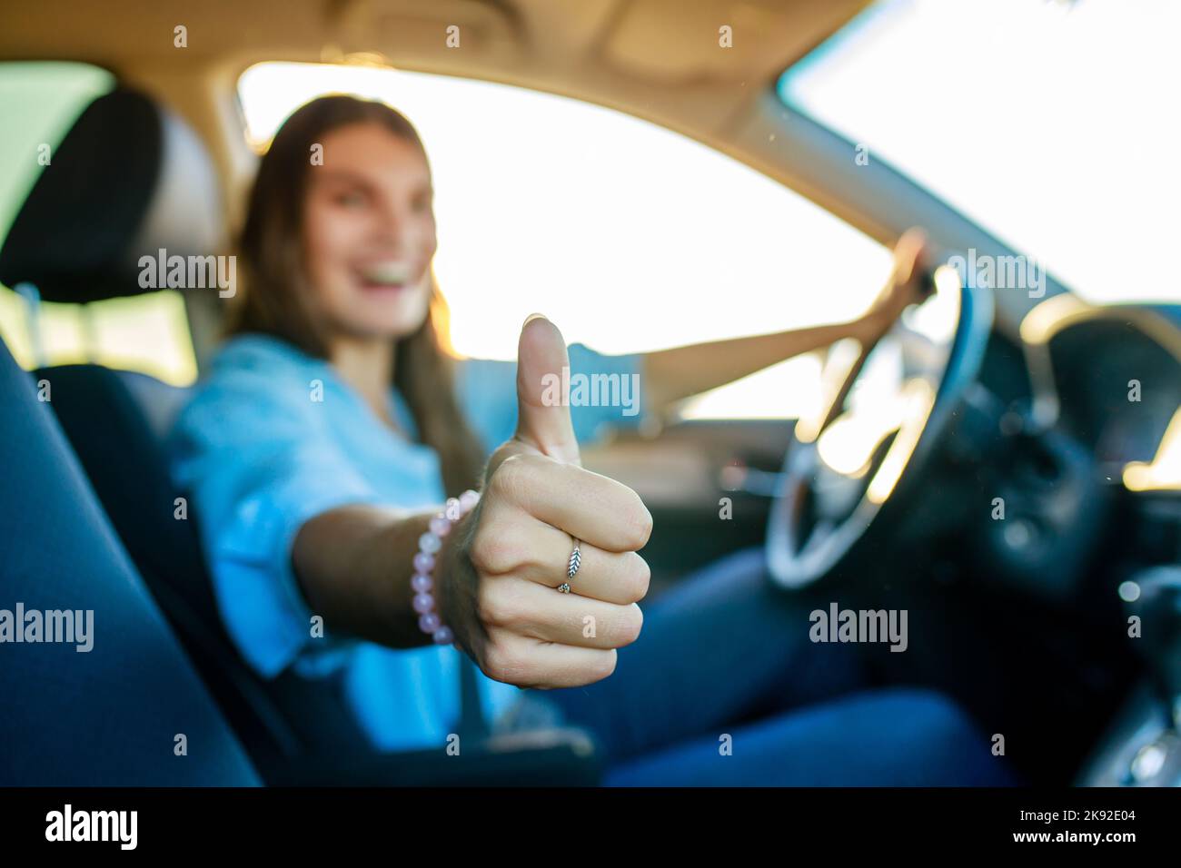 Beautiful happy woman driving her new car and showing thumbs up gesture ...