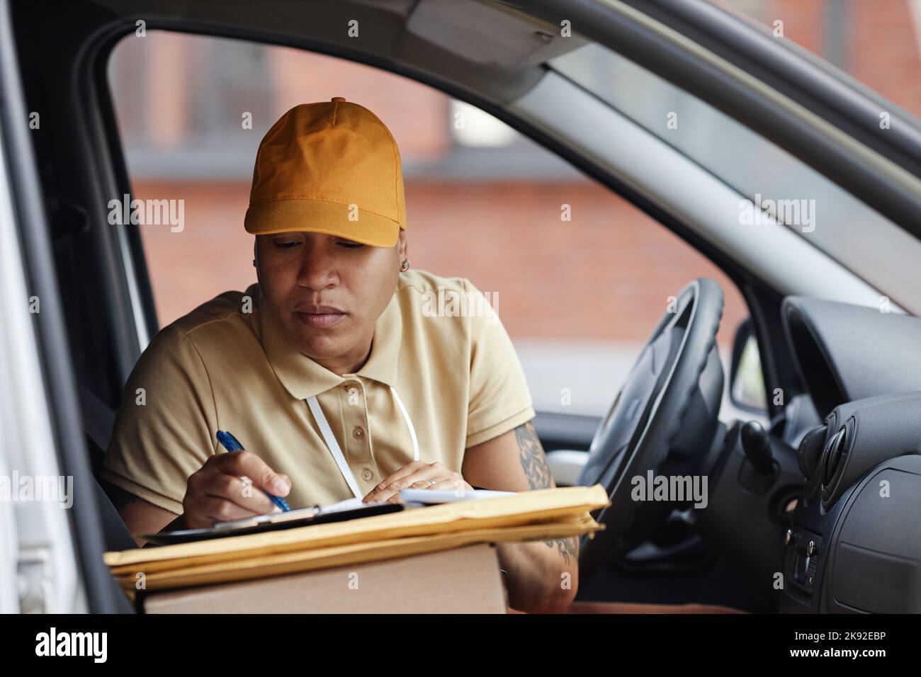 Portrait of young multiethnic woman driving delivery truck and filling ...