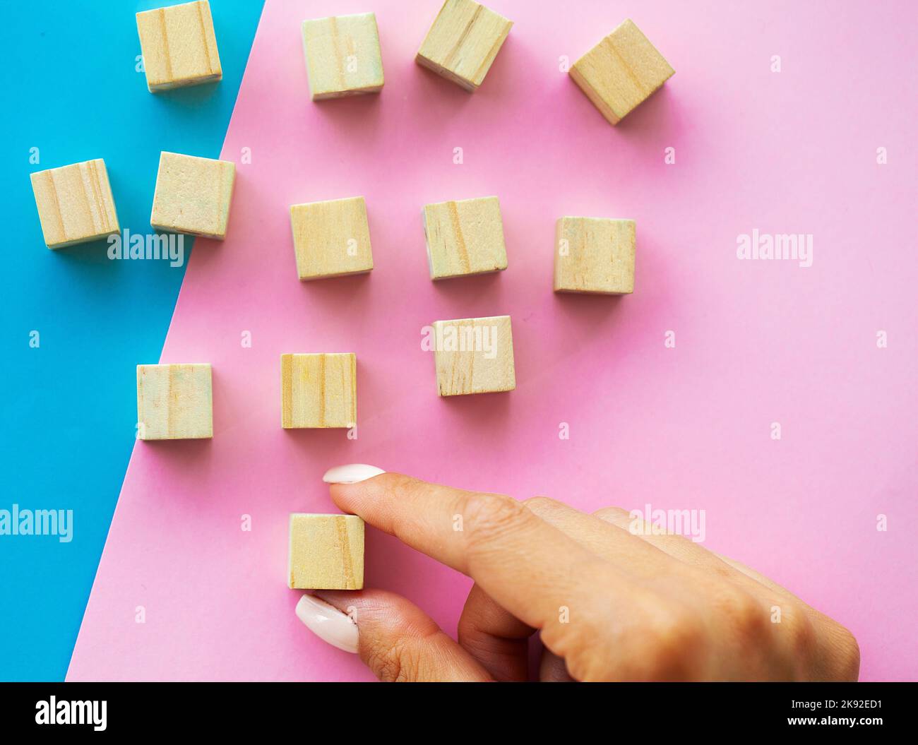Female hand arranging empty wood block and copy space on blue and pink ...