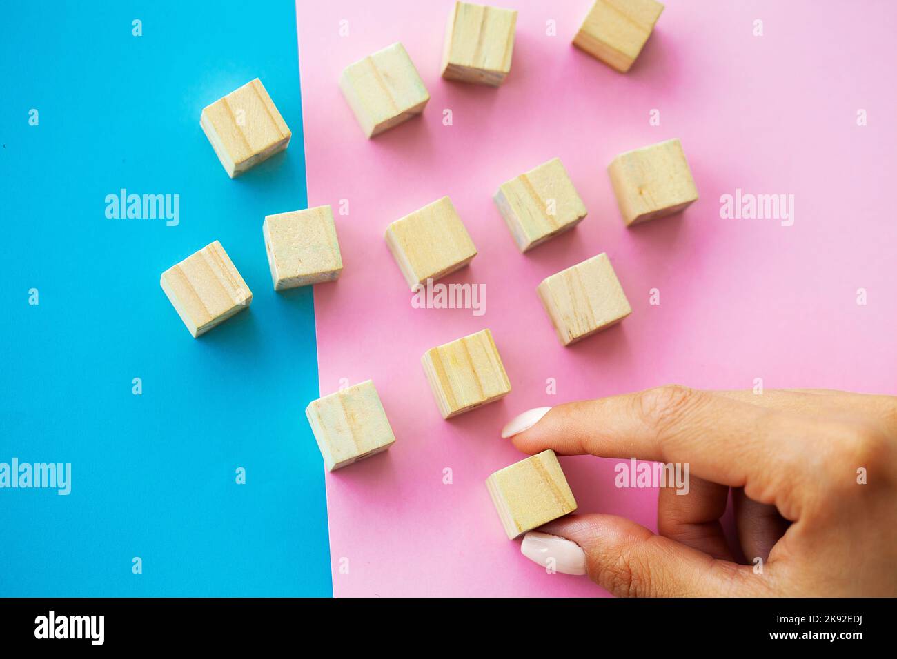 Female hand arranging empty wood block and copy space on blue and pink ...