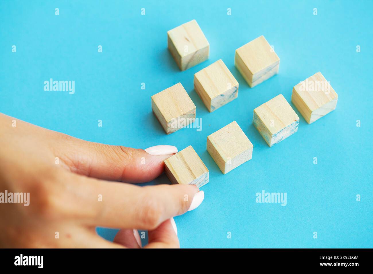 Wooden blocks with a human hand placing one cube at the top on blue ...