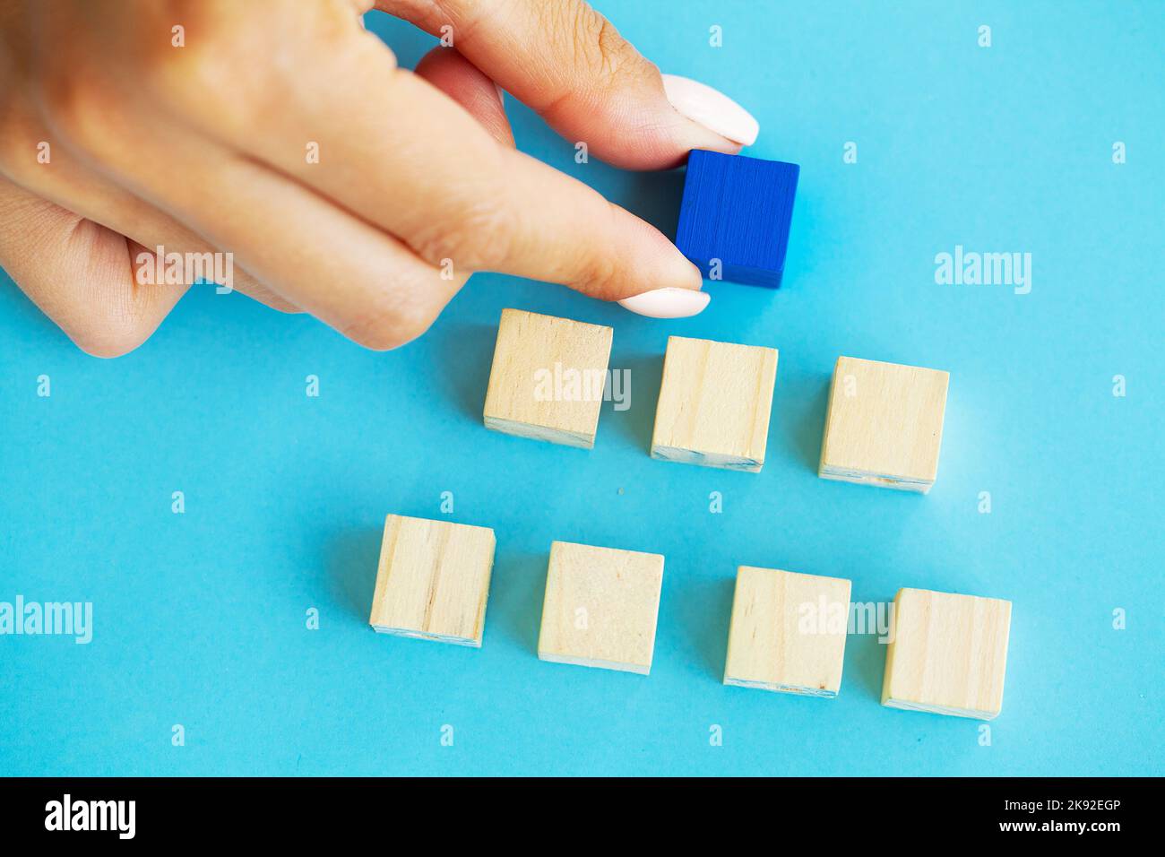 Wooden blocks with a human hand placing one cube at the top on blue ...