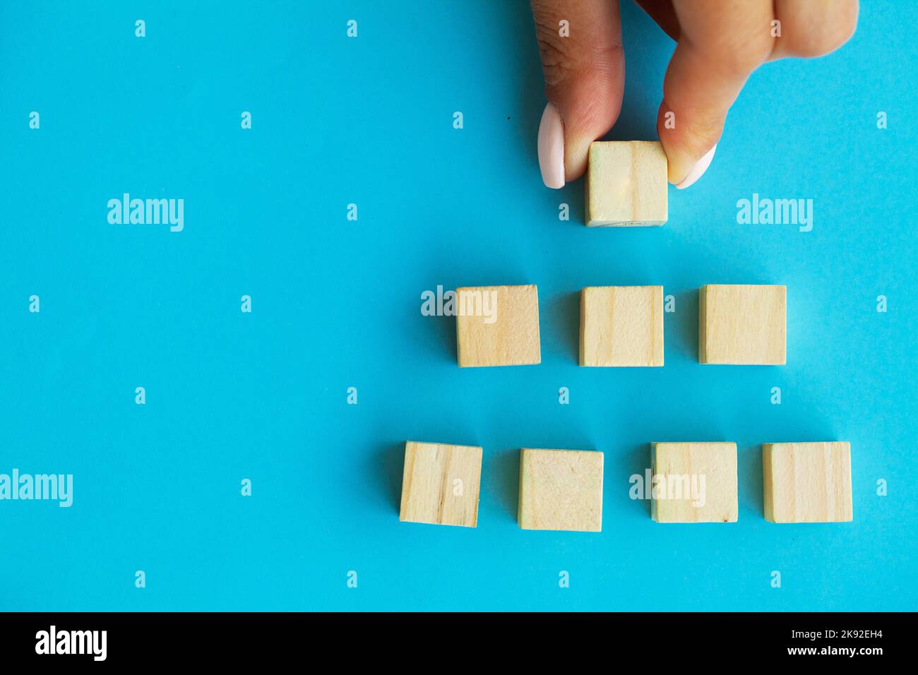 Wooden blocks with a human hand placing one cube at the top on blue ...