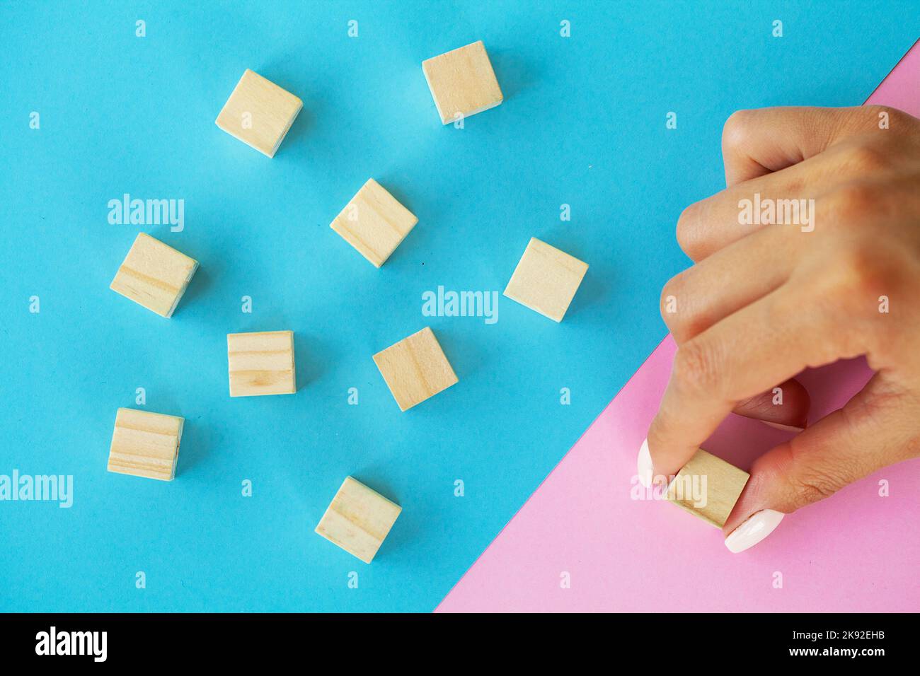 Female hand arranging empty wood block and copy space on blue and pink ...