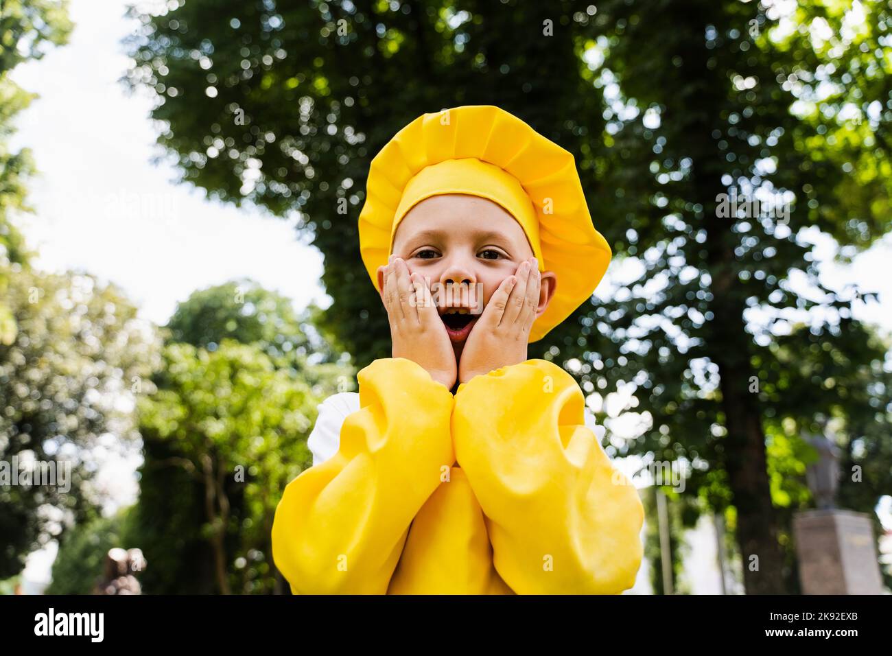 Shocked cook child in yellow chefs hat and apron yellow uniform holding ...