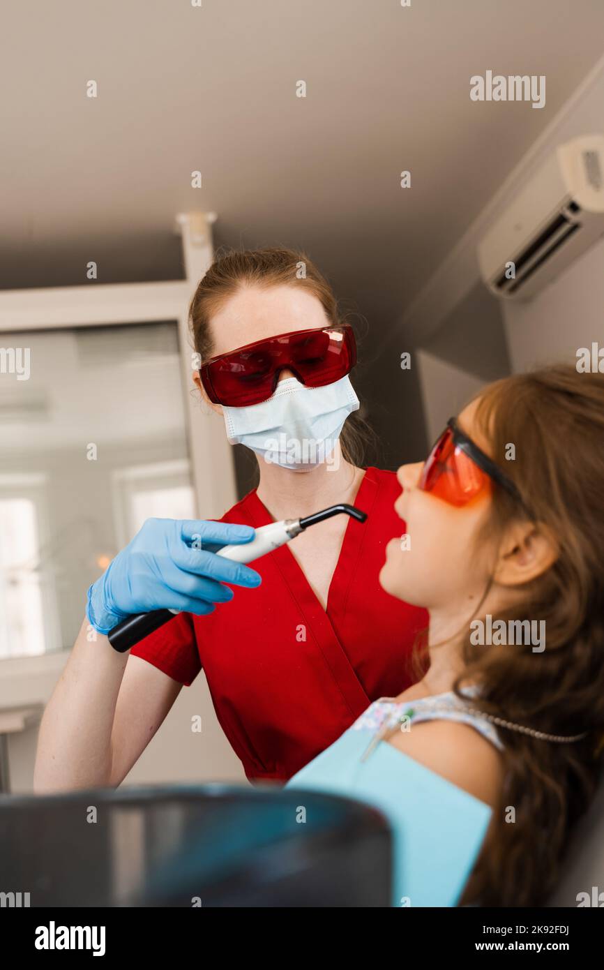 Child dentist treats and removes caries in a patient. Uv illumination of photopolymer tooth ...