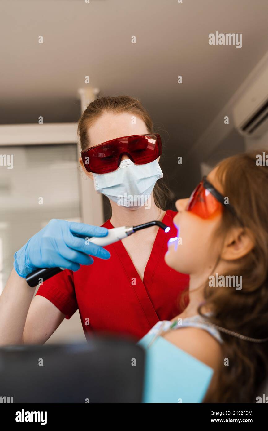 Child dentist treats and removes caries in a patient. Uv illumination ...