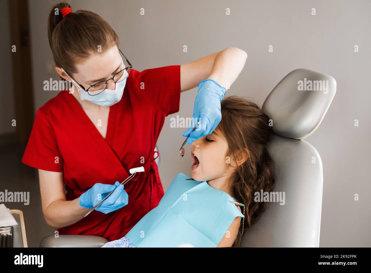Pediatric dentist puts cotton swab in mouth of a child girl to install ...