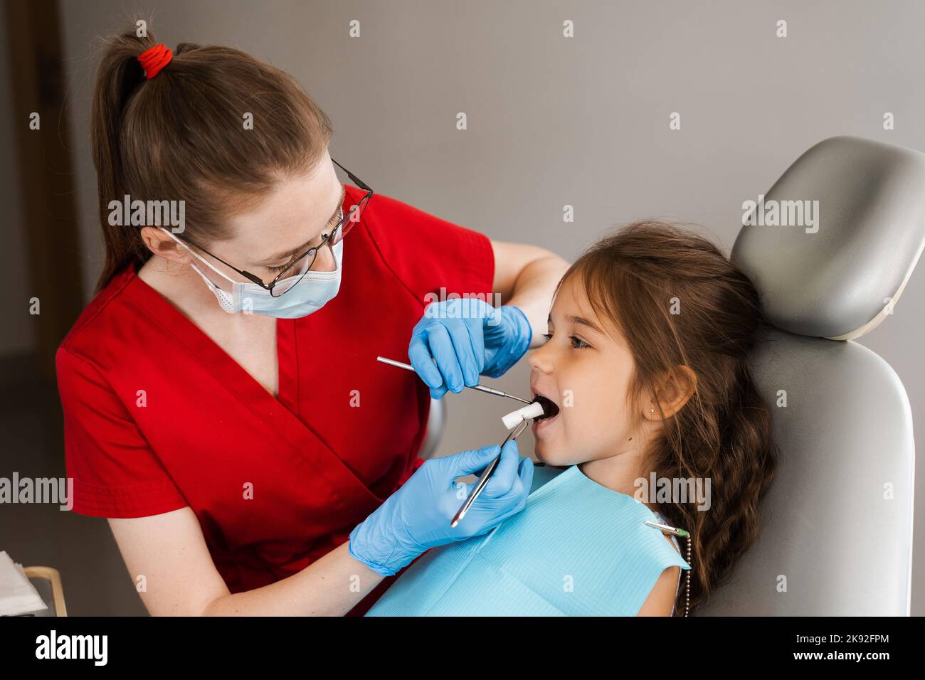 Pediatric dentist puts cotton swab in mouth of a child girl to install ...