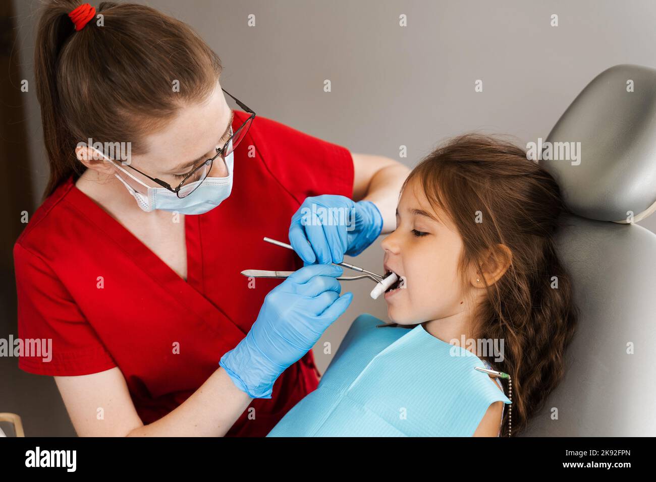 Pediatric dentist puts cotton swab in mouth of a child girl to install ...