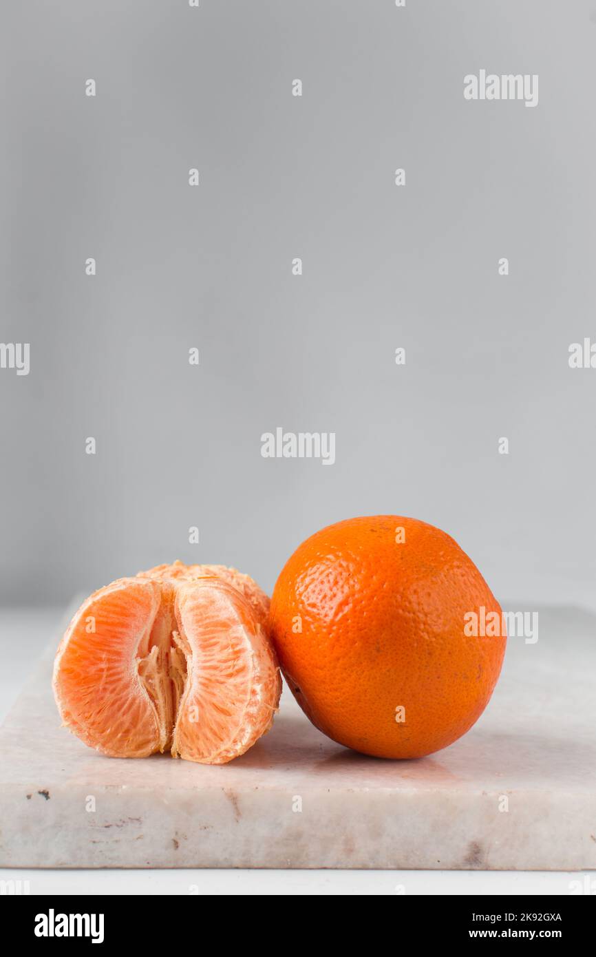 Peeled and unpeeled clementines on a marble chopping board, orange ...