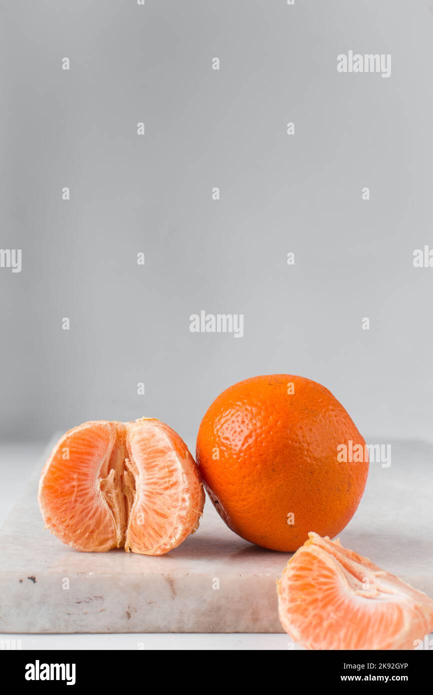 Peeled and unpeeled clementines on a marble chopping board, orange ...