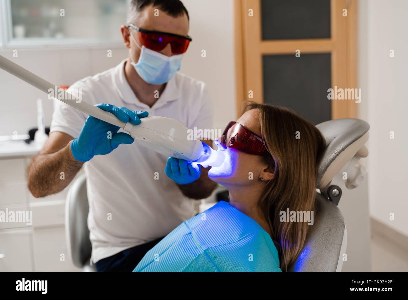 Artificial teeth whitening. Woman in red protective glasses patient do ...